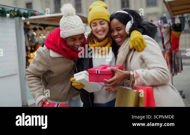 Friends exchanging festive gifts, laughing and smiling while shopping ...