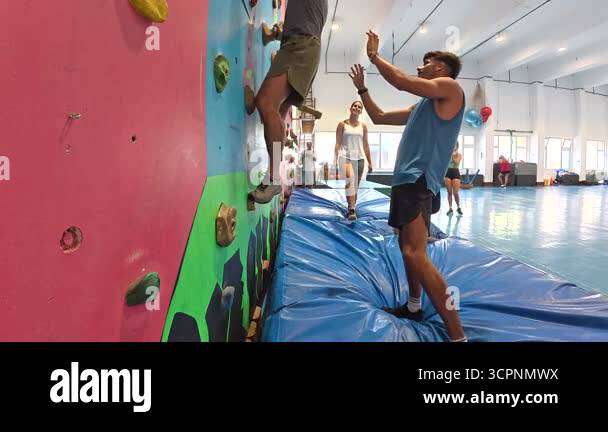 Professional gym instructor carefully spotting athletic climber during ...
