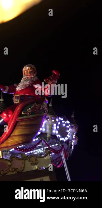 Santa claus waves joyfully from his sleigh on a carousel at a festive ...