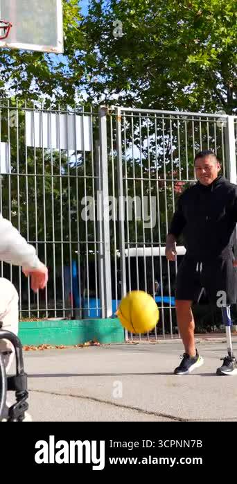 Two disabled friends playing basketball on an outdoor court, one with a ...
