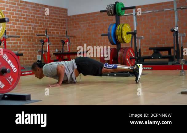 Determined male amputee with a prosthetic leg doing push ups in a gym ...