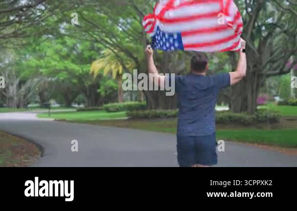 Sportsman carries American flag high while jogging on tree-lined road ...