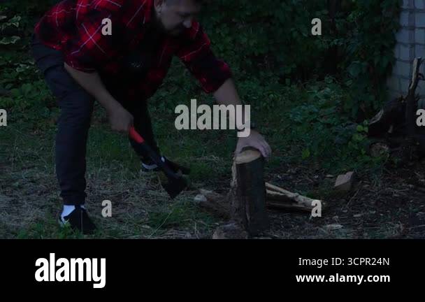4K video of a man in a checkered shirt chopping logs with an axe near a ...