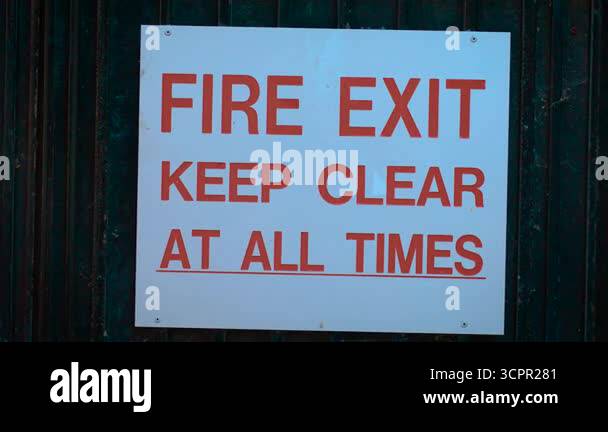 Sign stating fire exit mounted on metal gate beside tiled wall. Board ...