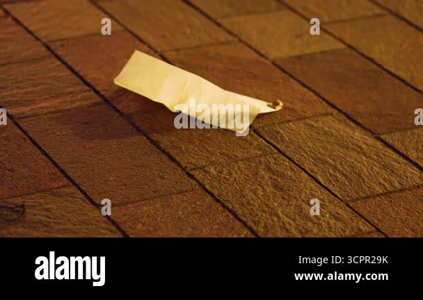 Crumpled paper fluttering and sliding over dimly lit pavement. Light ...