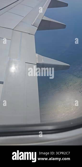 Aircraft flying above shimmering sea surface, view from window porthole ...