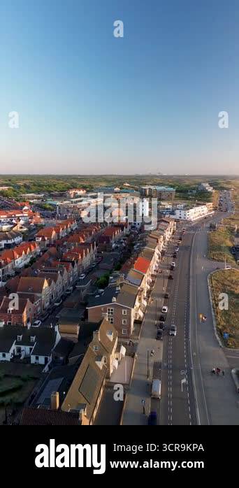 Aerial view of a coastal town with red and brown rooftops, a wide road ...