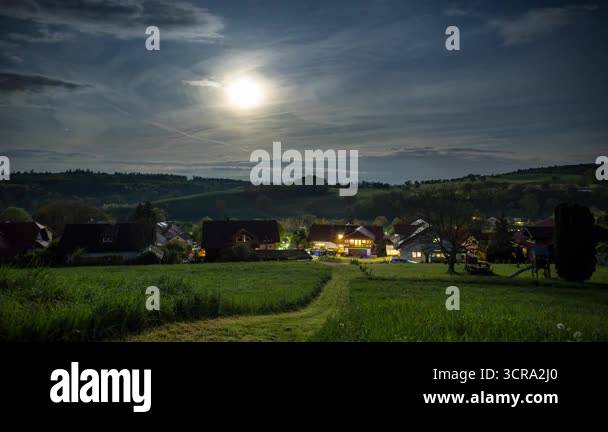 Bright evening summer sun in gray-blue cloudy sky illuminates a small ...