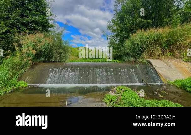Scenic view of a small river waterfall flowing over a concrete weir ...