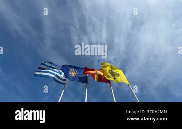 Four iconic flags waving together against the sky: the national flag of Greece, the regional ...