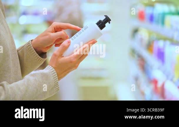 Close-up of female customer holding a cosmetic bottle and reading the ...