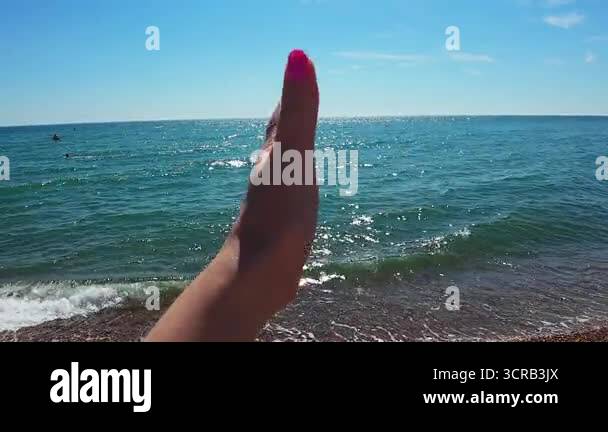 A closeup of a womans hand with pink nails reaching out to the ocean ...