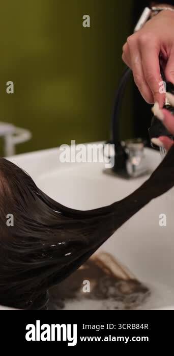 Closeup detail of hairstylist washing hair with water at sink during ...