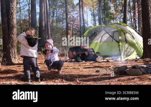 Two children play near the campfire while their family sets up a tent ...