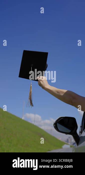 A Caucasian woman waves her graduation cap while extending her arms out ...