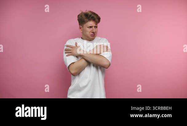 A person stands in a pink room wearing a t-shirt, visibly shivering ...