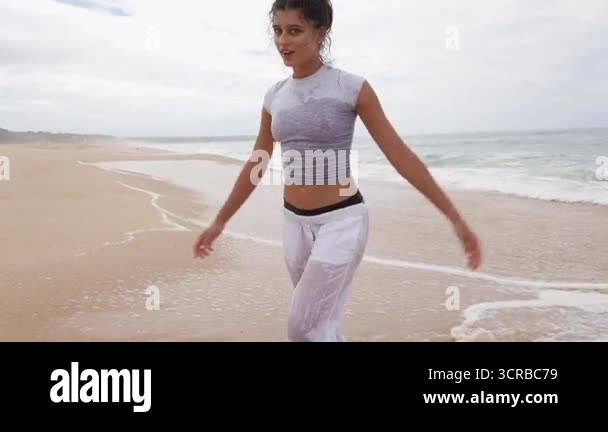 A young woman joyfully walking along a serene beach, fully embodying ...