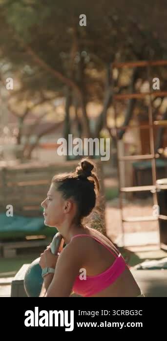 A fit woman performs kettlebell squats in a vibrant outdoor gym ...