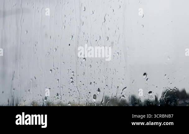 Closeup of rain hitting window with water drops streaming down the ...