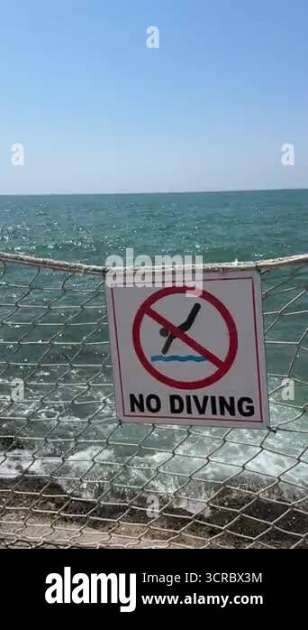 Vertical video of a No Diving sign on a seaside safety fence with ocean ...