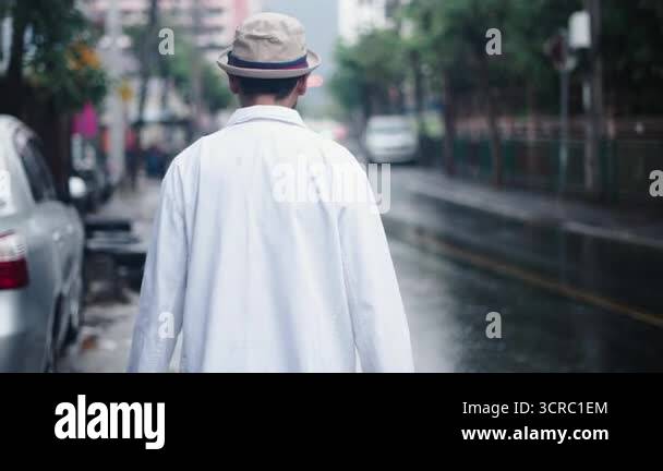 Man walking down a city street in the rain, carrying groceries in ...