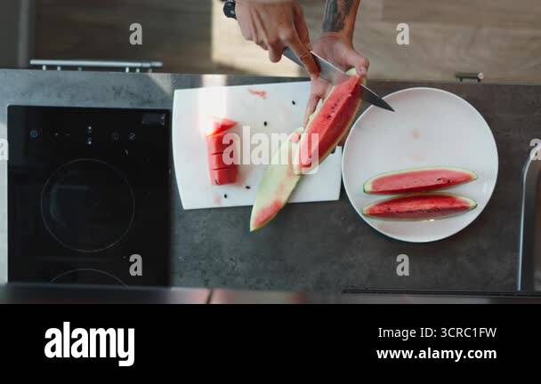 Chef expertly cuts watermelon slices on a white cutting board, placing ...