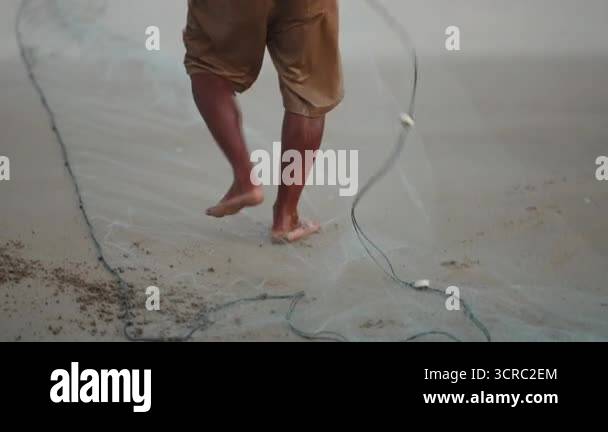 Fisherman walks barefoot on the beach on wet sand pulling fishing net ...