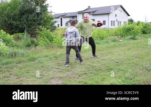 Adult coach demonstrates punch while boy dodges during boxing training ...