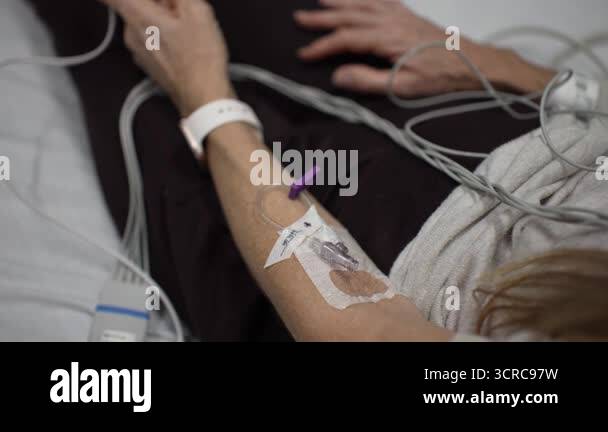 A mature woman is lying in a hospital bed connected to heart monitors and EKG equipment ...