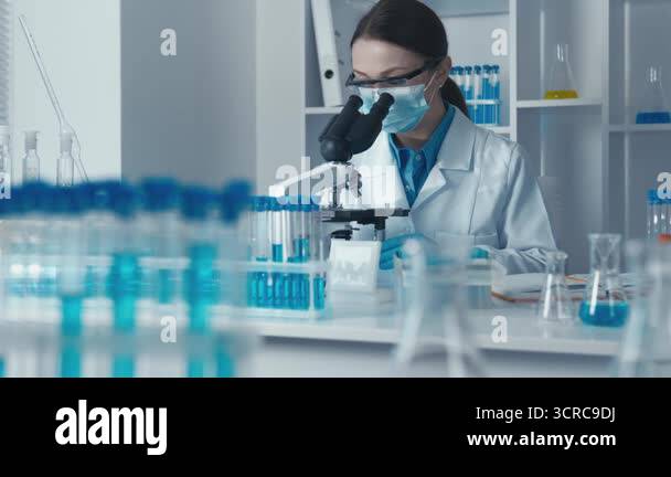 A dedicated scientist in a white lab coat examines samples under a ...