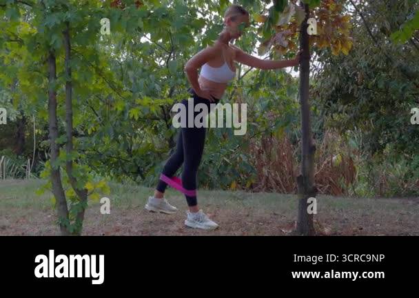 Young fit woman in sports bra and leggings exercising with resistance ...