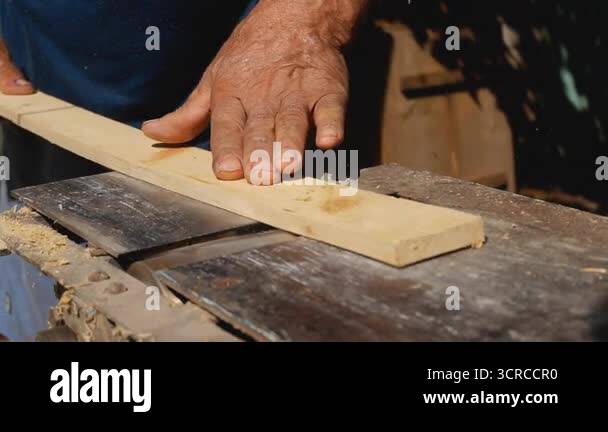 A mans hand runs a wooden plank through a woodworking machine that ...