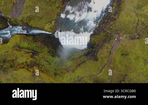 A powerful waterfall flows into a rocky basin surrounded by moss and ...