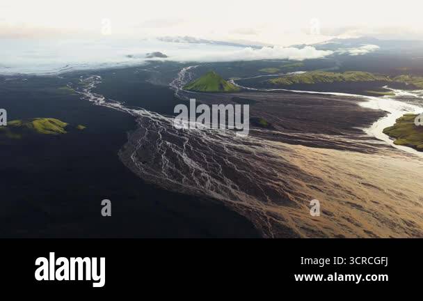 Aerial view of braided rivers flowing across dark volcanic plains, with ...