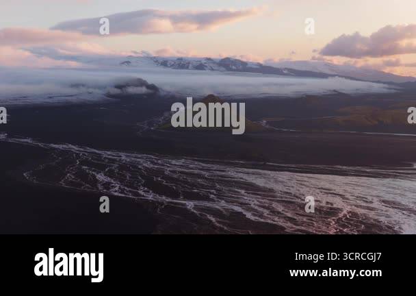 Drone captures a green pyramid shaped mountain, glacial rivers on black ...