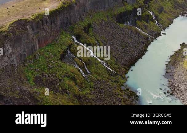 Aerial view of a waterfall in Iceland flowing over moss covered rocks into a turquoise river ...