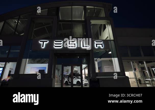 Exterior sign of Tesla dealership with sunny evening sky. The ...