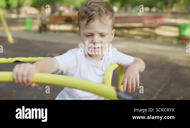 Serious boy sits on playground carousel gripping yellow bar with both ...