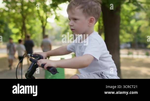 Happy blond boy rides bicycle in park pedalling forward with steady ...
