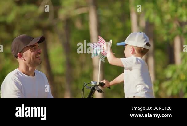 Happy dad smiles while preschooler son blows air at colorful pinwheel ...