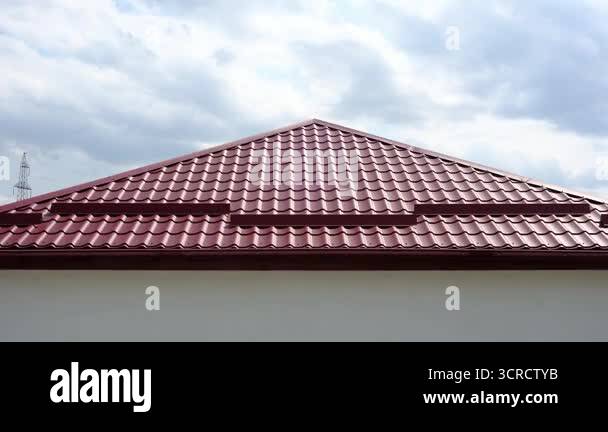Red metal roof tiles cover a building against a cloudy blue sky ...