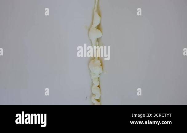 Expanding foam sealant fills a vertical gap on a textured white wall ...