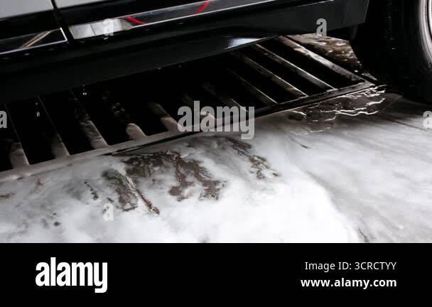 Dark vehicle wheel and side step above metal drain grate with white ...