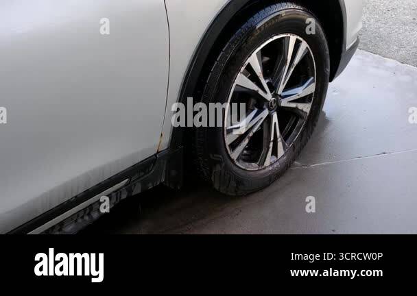 Close view of white passenger car side. Wet black tire and shiny metal ...