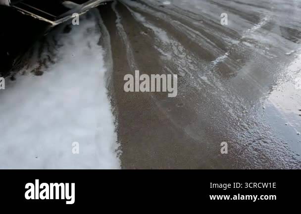 White foam spreads over a dark wet concrete floor. Soapy bubbles flow ...