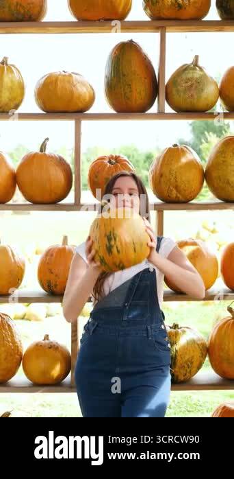 Young woman holding a large pumpkin over her head amidst a display of ...