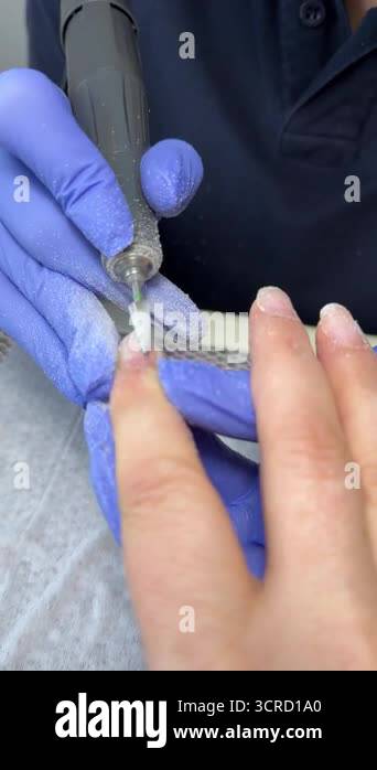 Nail technician using an electric file to shape and prepare a client ...