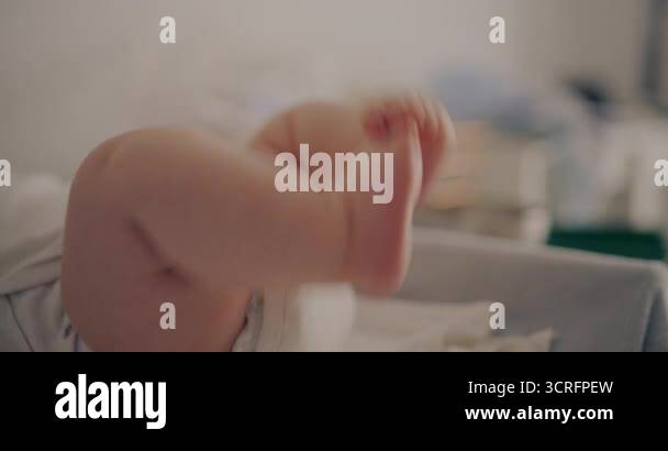 Adorable baby boy lifting his legs joyfully on a changing table, moving ...