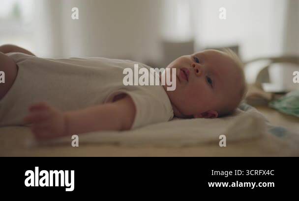 Adorable baby boy lying on a changing table, moving arms and legs while ...