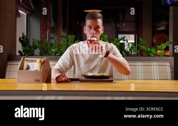 Young man sitting at restaurant table with beer glass and meal, cozy ...